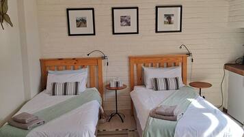 Quarto com duas camas, uma mesinha e um painel com três quadros.