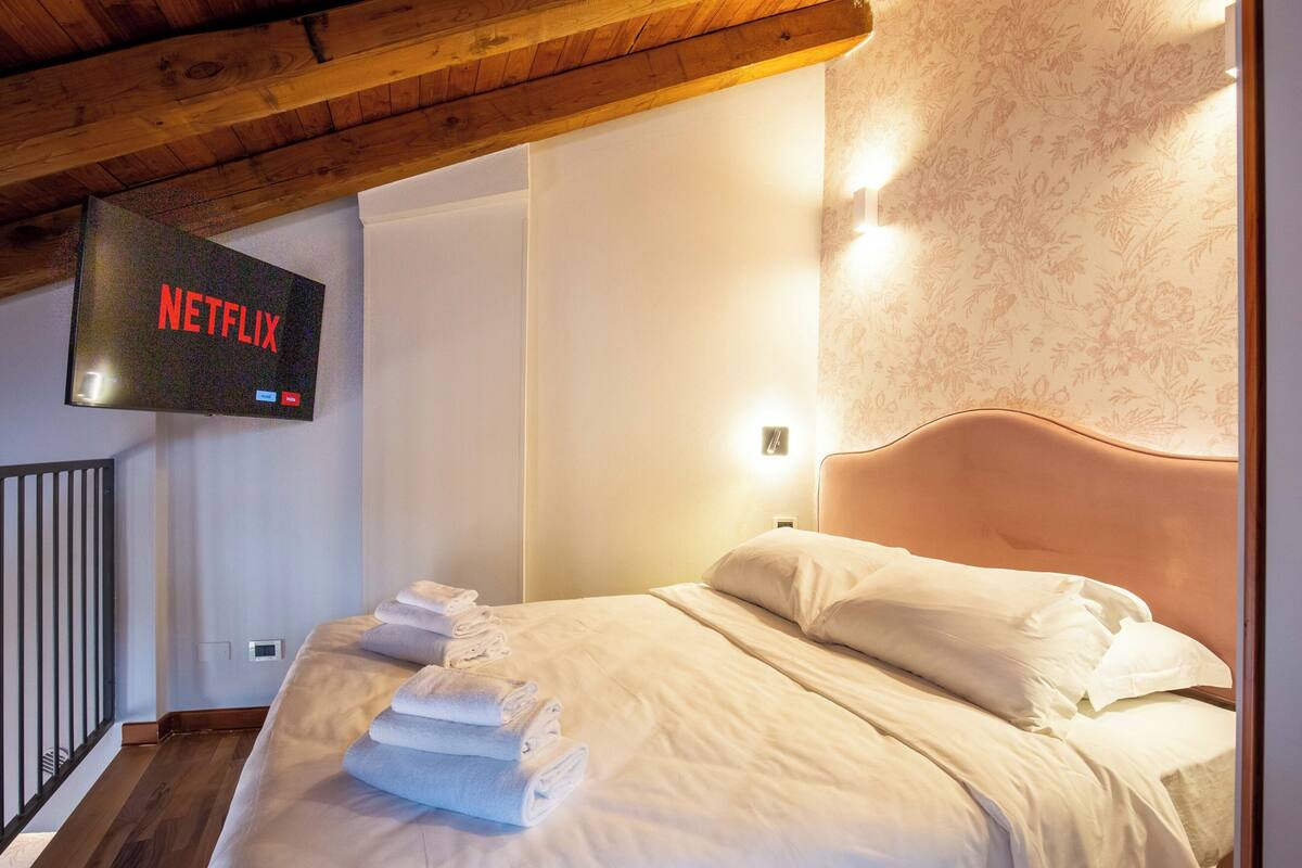 Quarto de hotel com uma cama, televisão de tela plana na parede e teto de madeira.