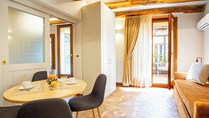 Quarto de hotel com teto de madeira, área de refeições com mesa e cadeiras, um sofá e vista para o exterior.