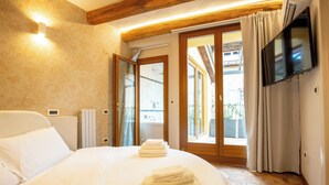 Quarto de hotel com cama, televisão e varanda com cortinas.