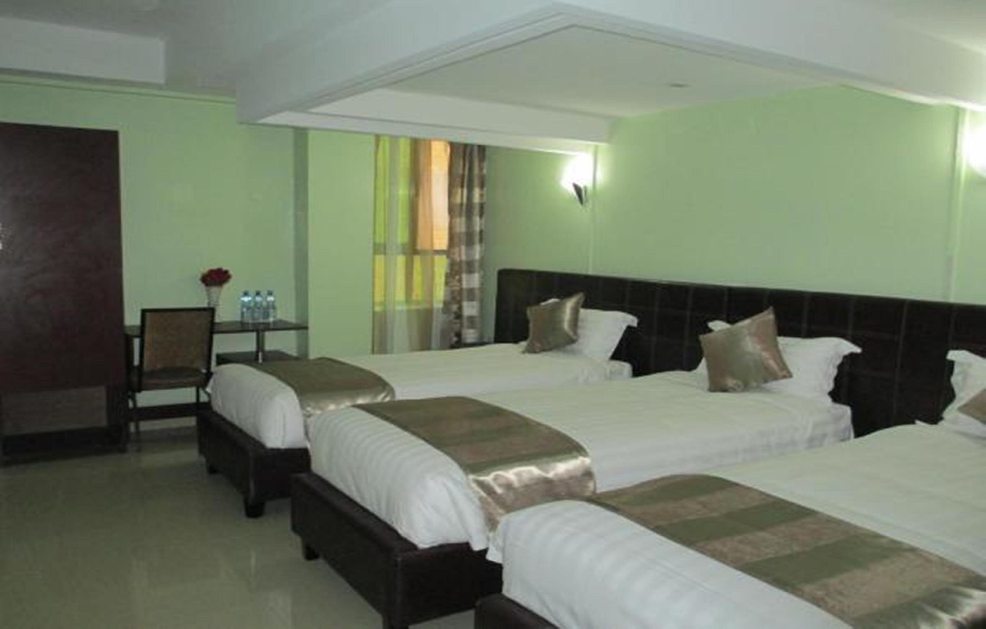 Quarto de hotel com duas camas, uma mesa pequena com uma cadeira e um vaso com flores.