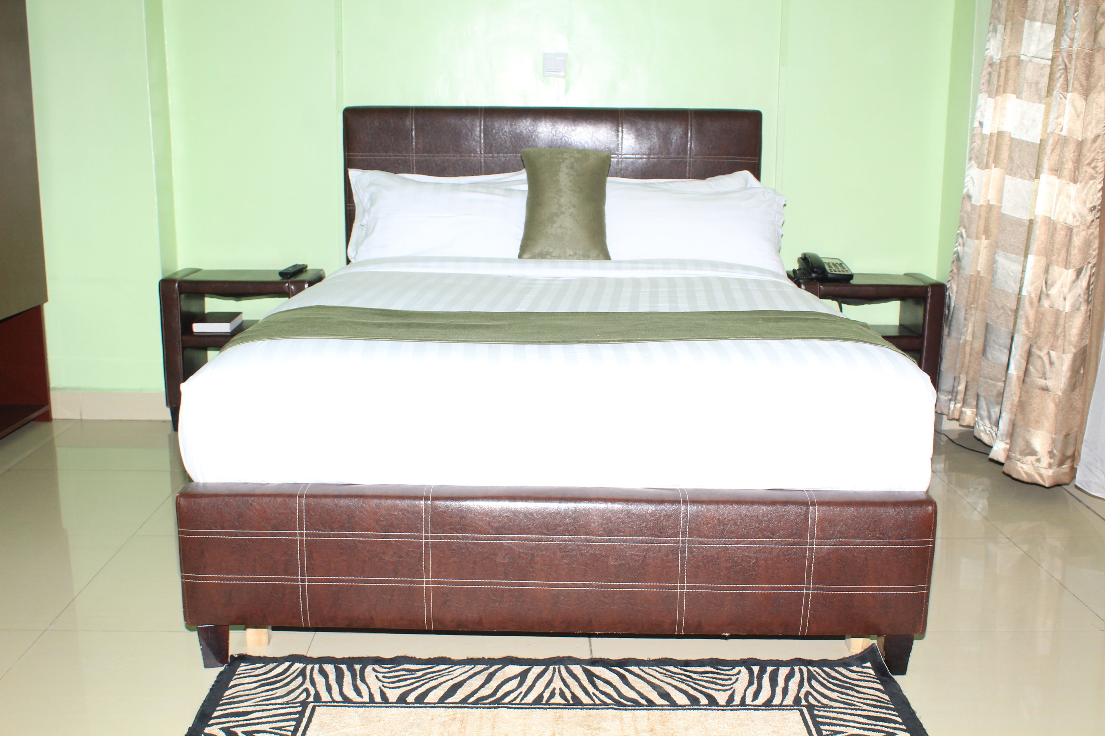 Cama bem arrumada com cabeceira, duas mesas de cabeceira com telefones e um tapete estampado com padrão de zebra.