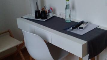 Uma pequena mesa branca com uma cadeira, uma garrafa de água, um telemóvel e um rolo de papel de cozinha.