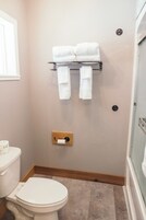 Casa de banho com sanita, um porta-toalhas com toalhas, um rolo de papel higiénico e zona de duche.