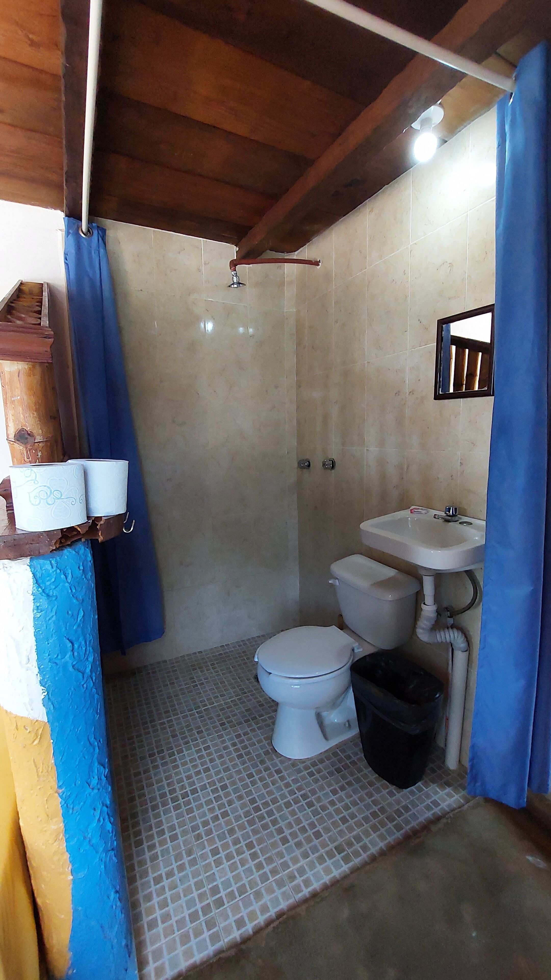 Casa de banho pequena e revestida a azulejos, com sanita, lavatório e zona de duche.