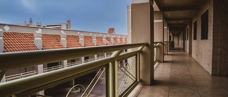 Um corredor com piso de azulejos, corrimão de metal e vista para edifícios com telhados de terracota.