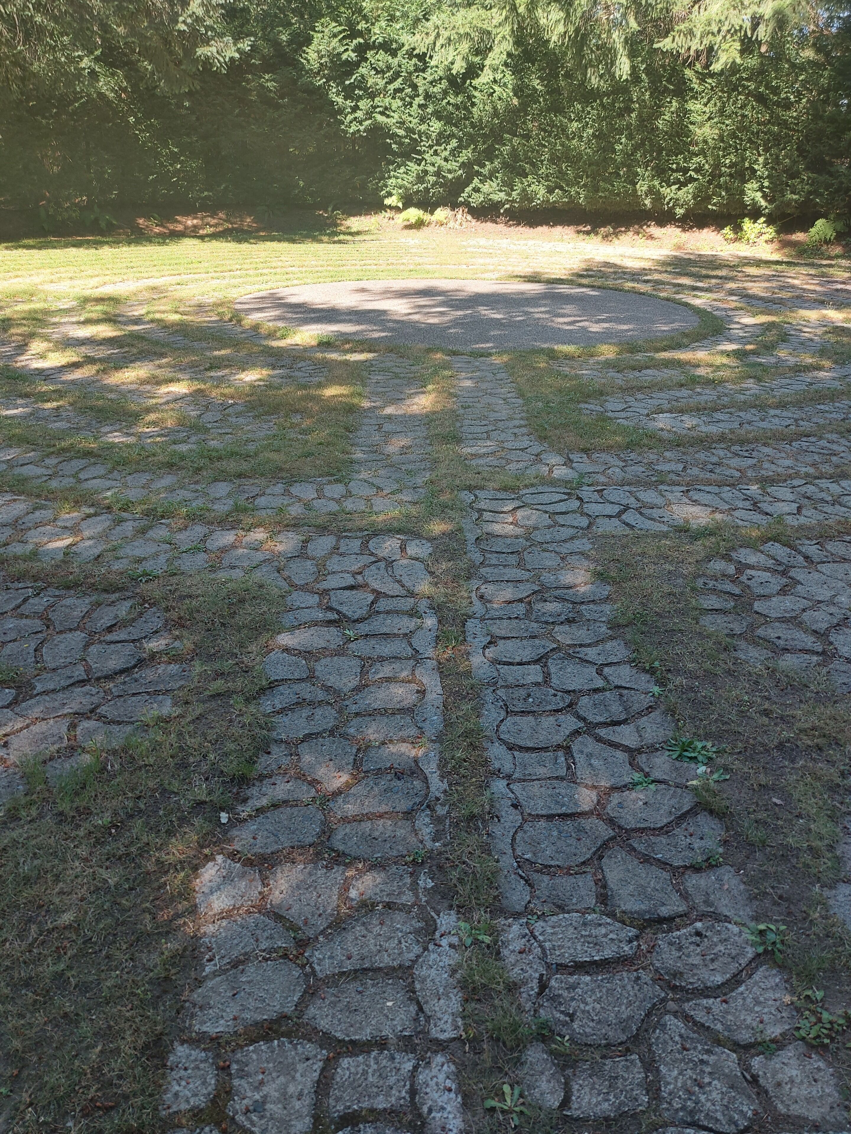 Um caminho pavimentado com pedras irregulares, ladeado por grama e árvores.