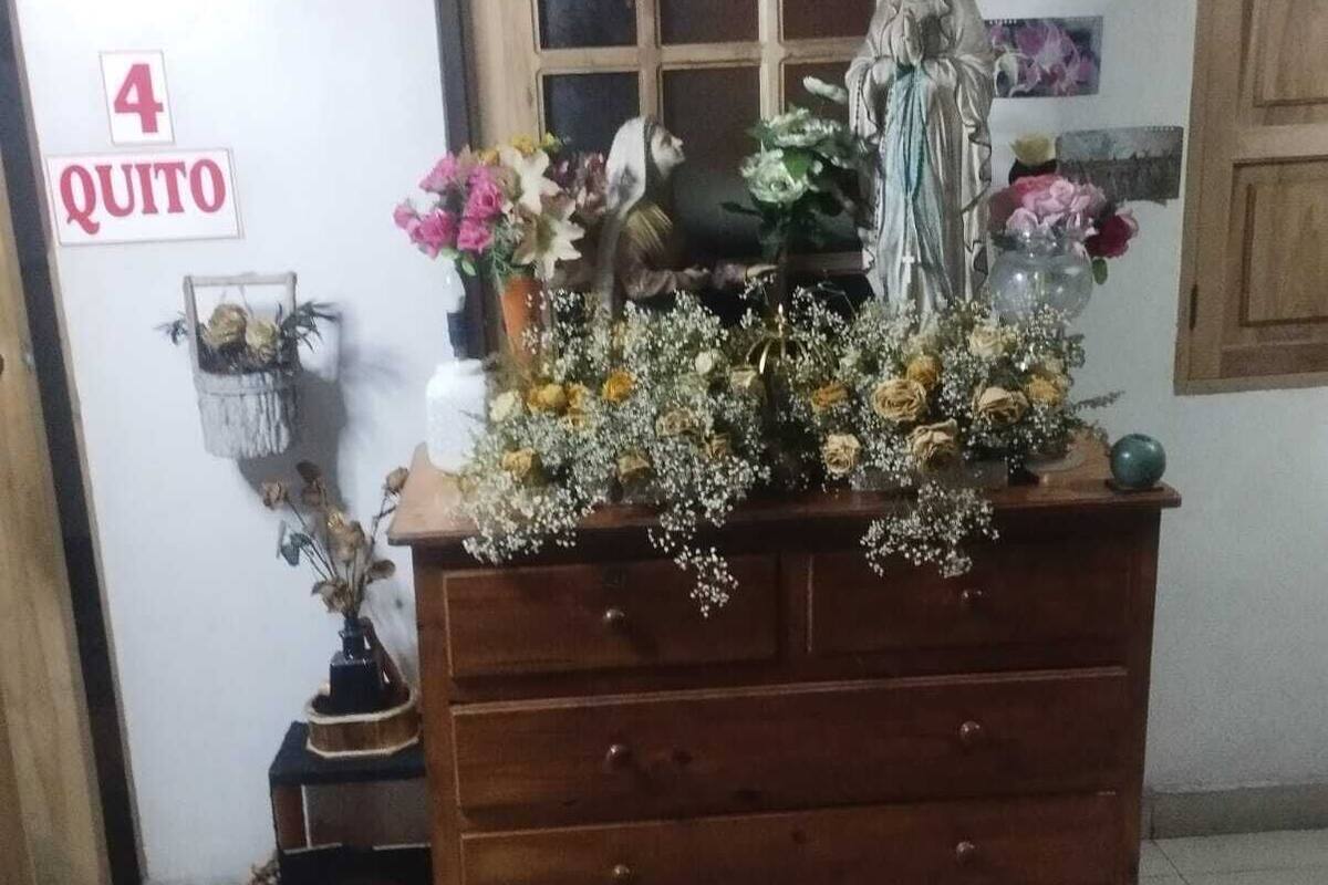 Uma cômoda de madeira com uma estátua e flores, uma porta com uma placa, e uma janela com vista.
