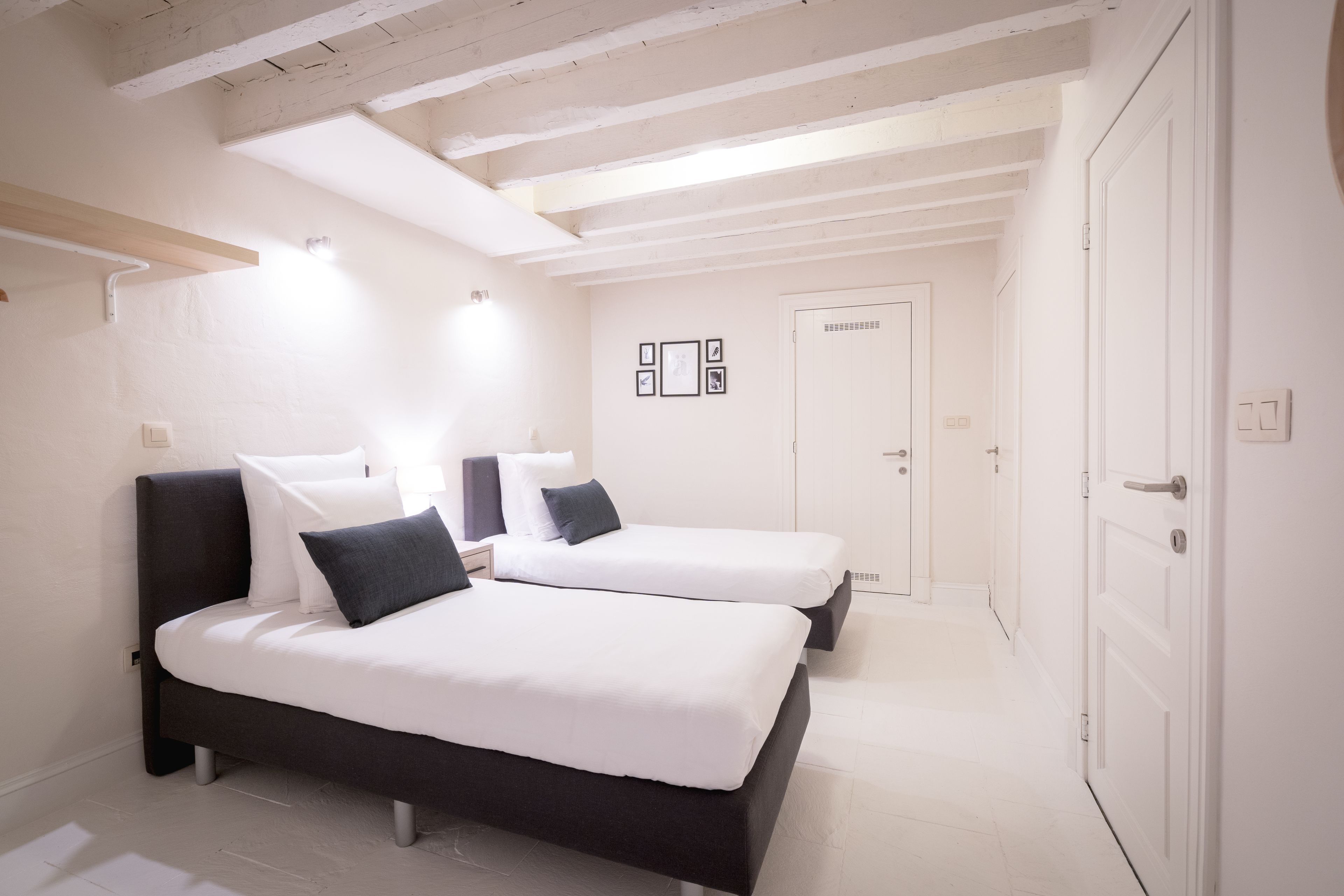 Quarto de hotel com duas camas, paredes brancas e uma porta ao fundo.
