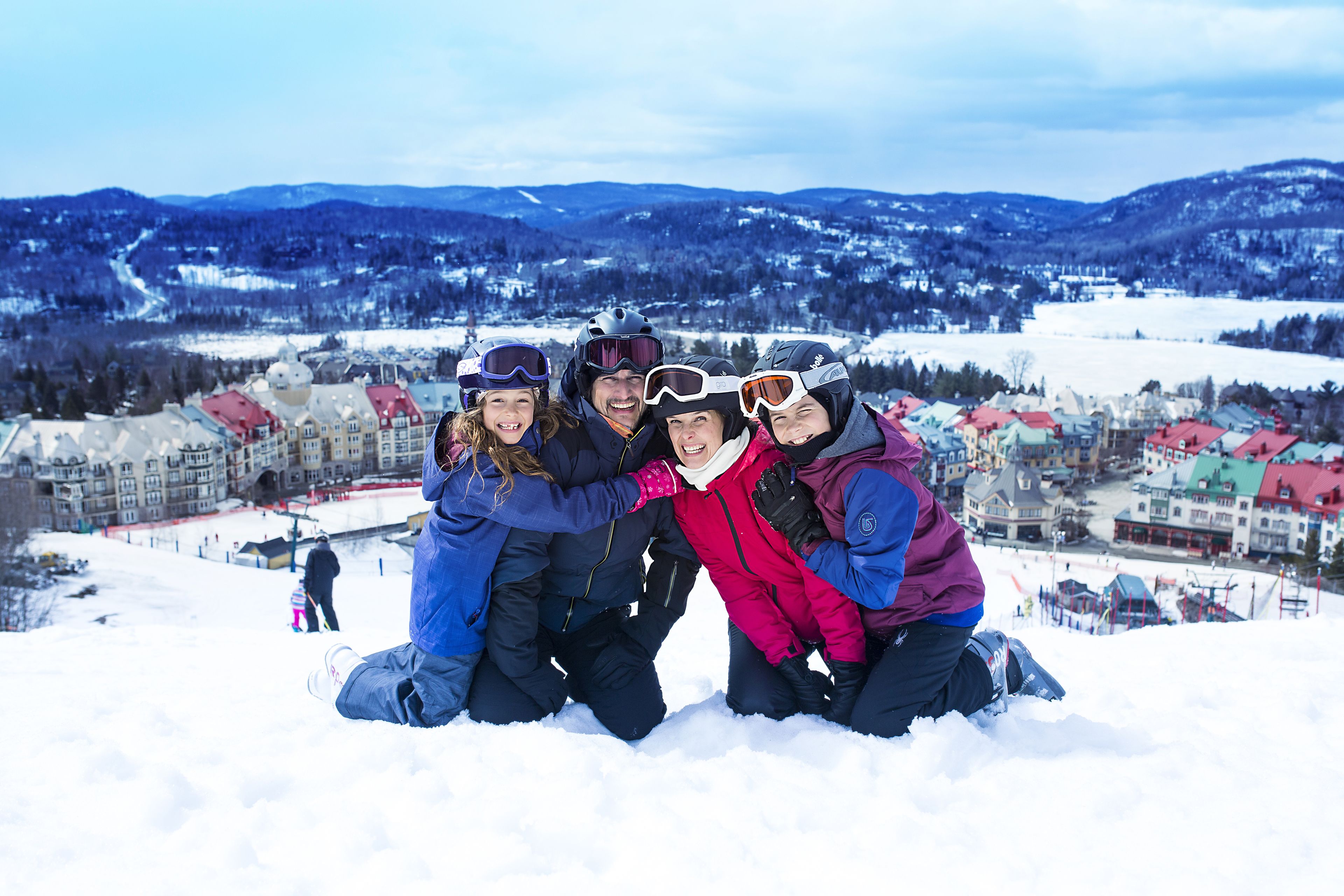 Um grupo de pessoas numa encosta coberta de neve, com uma cidade ao fundo.