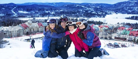 Um grupo de pessoas numa encosta coberta de neve, com uma cidade ao fundo.