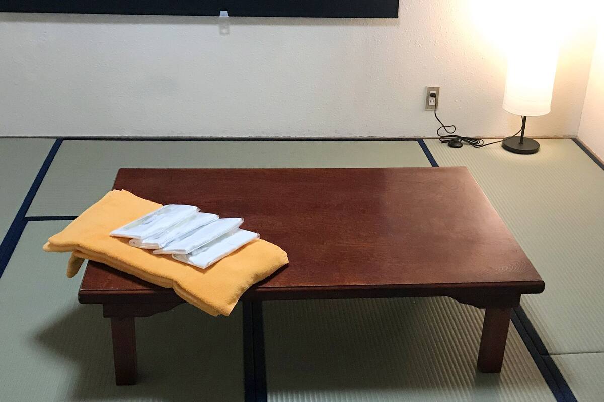 Um espaço com esteiras de tatame, uma mesa de madeira e uma lâmpada.