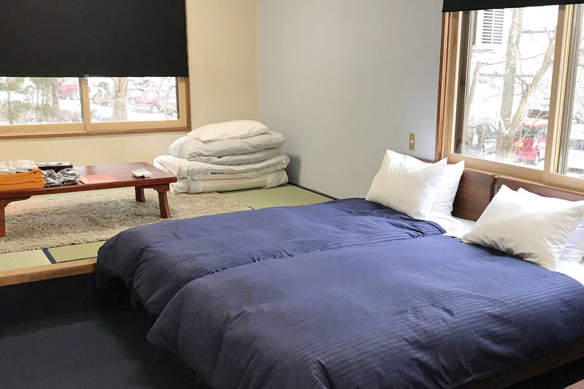 Um quarto com uma cama, uma mesinha e uma janela.