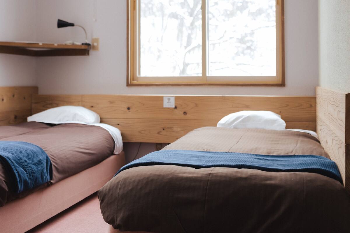 Quarto com duas camas, janela e prateleira com abajur.
