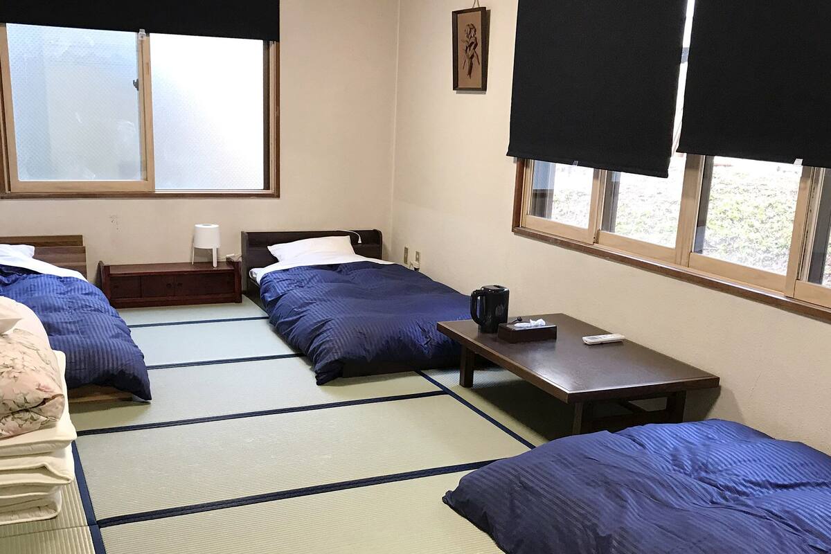 Quarto com duas camas, uma mesinha com chaleira, abajur e janela com vista para o exterior.