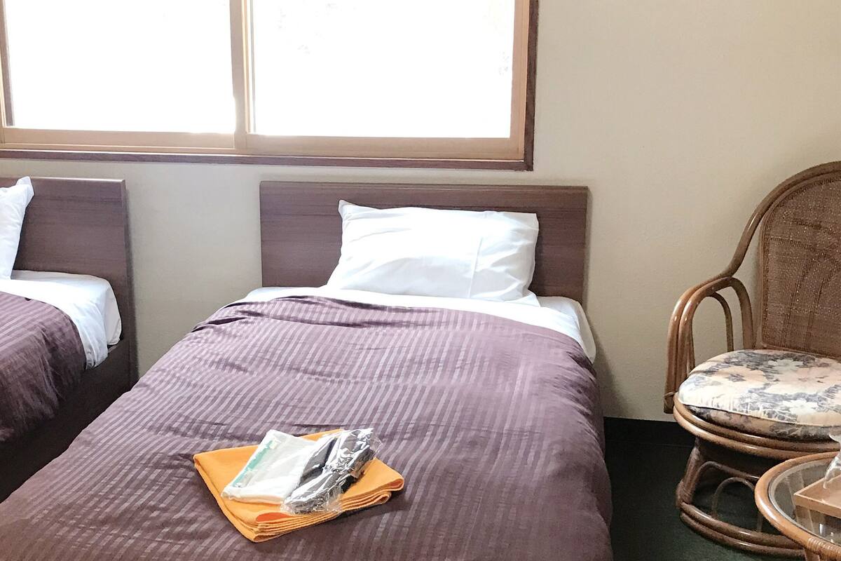Quarto de hotel com duas camas, uma cadeira e uma janela.