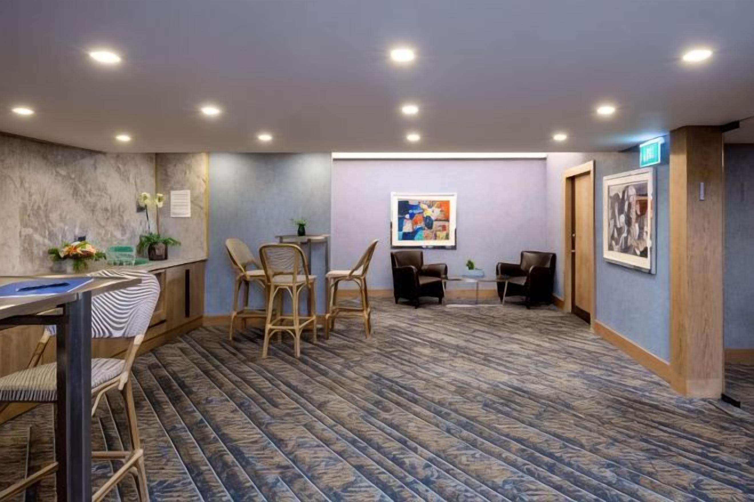 Um hall de hotel com balcão de recep ção, área de estar e piso coberto por carpete.