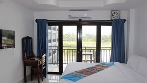 Quarto de hotel com cama, escrivaninha e cadeira. Possui varanda com vista para vegetação.