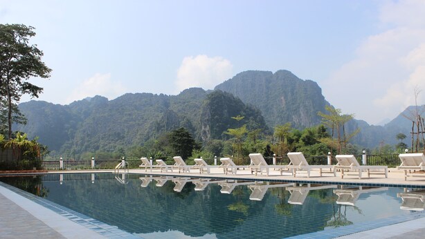 Piscina com espreguiçadeiras e montanhas ao fundo.
