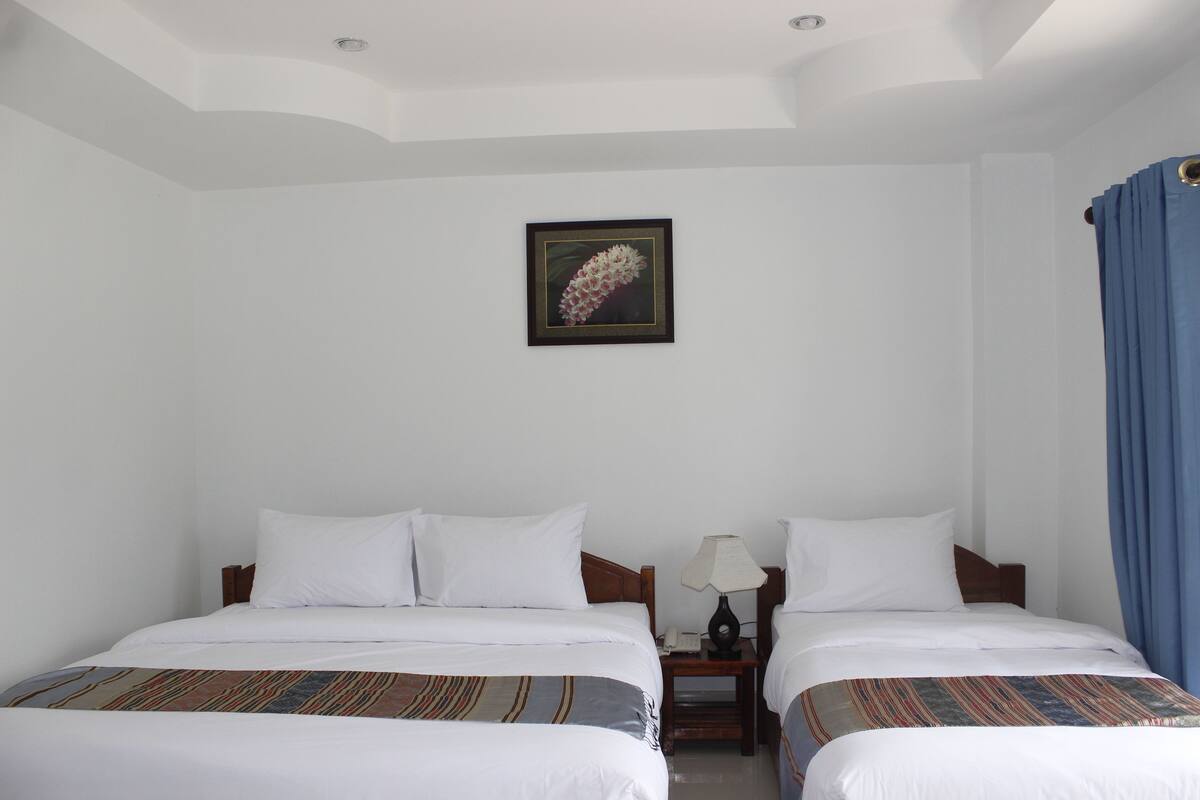 Quarto de hotel com duas camas, uma mesinha de cabeceira com abajur e um quadro na parede.