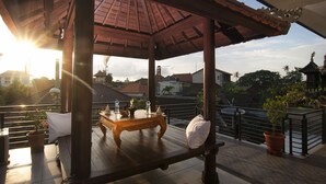 Um gazebo de madeira com telhado de azulejos, com vista para uma área residencial com casas e palmeiras.