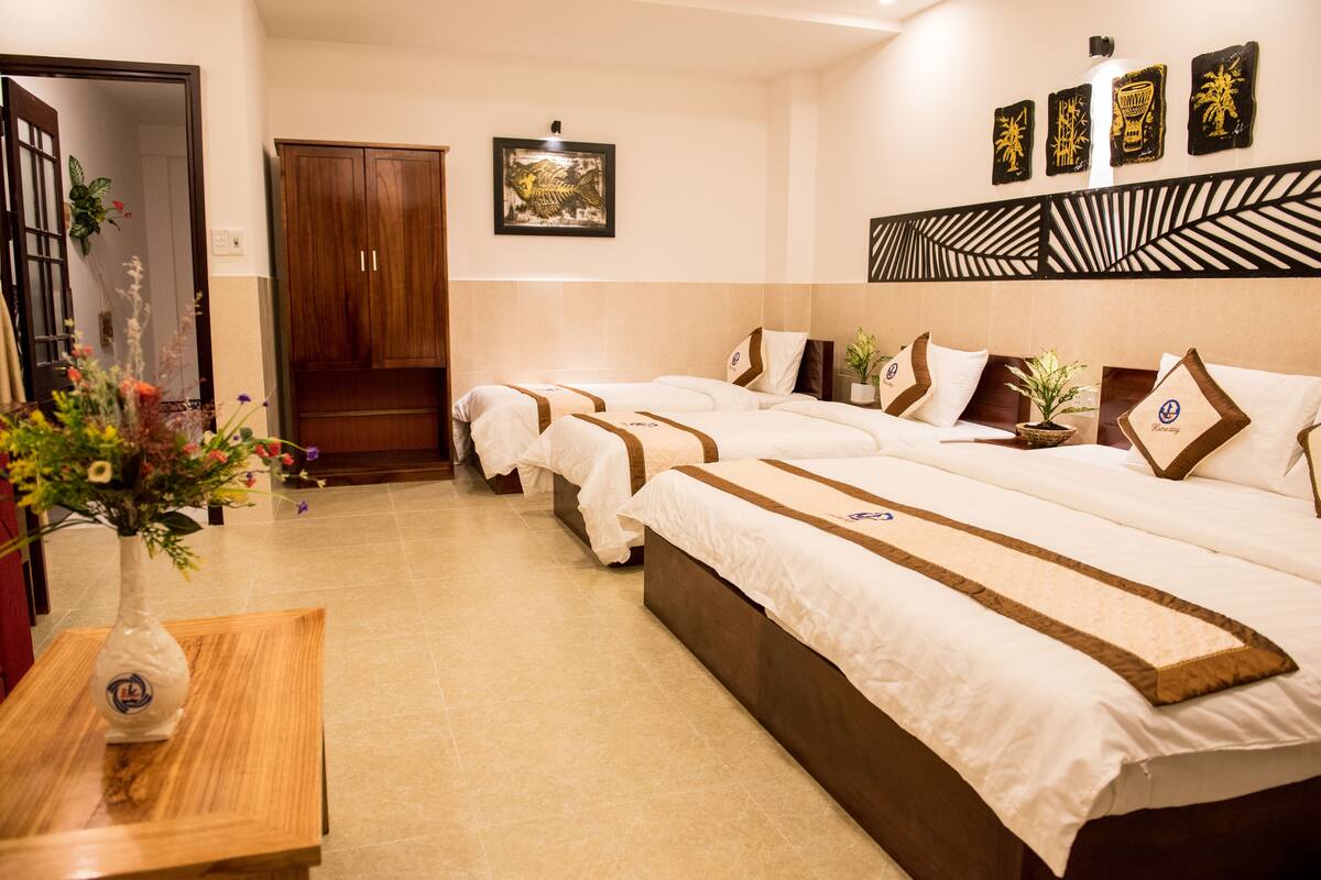 Quarto de hotel com três camas, um armário de madeira, um vaso com flores e um quadro na parede.