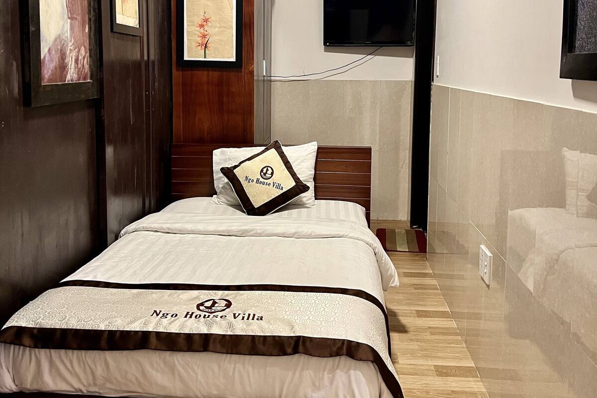 Um quarto com uma cama, uma mesa de cabeceira de madeira com um vaso, uma TV de tela plana e obras de arte emolduradas na parede.