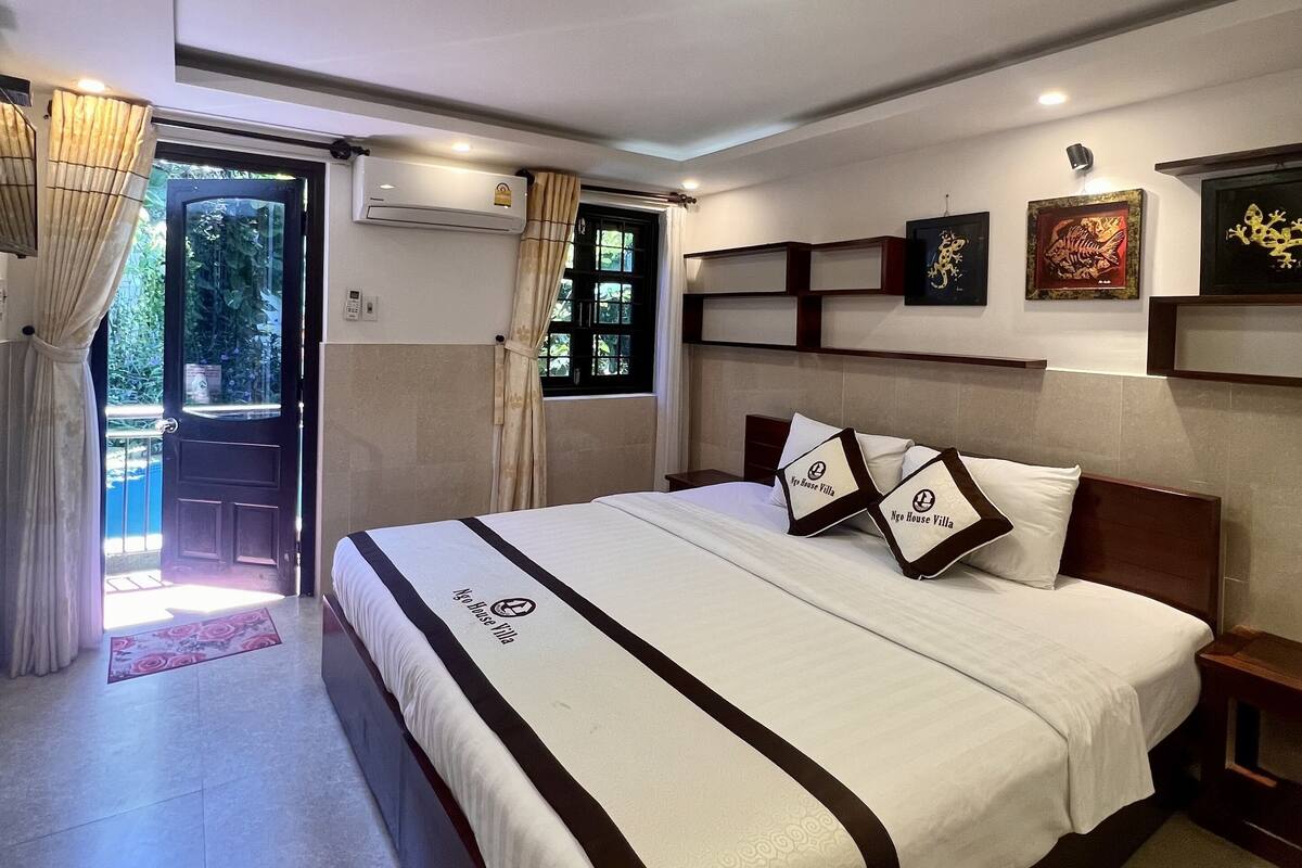 Quarto de hotel com uma cama grande, mesa de cabeceira, cortinas em uma janela e obras de arte na parede.