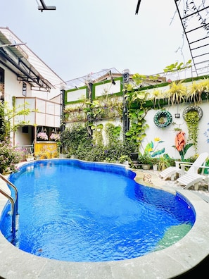 Piscina com borda azulejada, rodeada por vegetação exuberante e plantas.