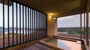 Varanda com piso de madeira e banheira de pedra quente, com vista para a água e vegetação.
