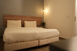 Cama com cabeceira de madeira, roupa de cama branca e uma planta na mesa de cabeceira.