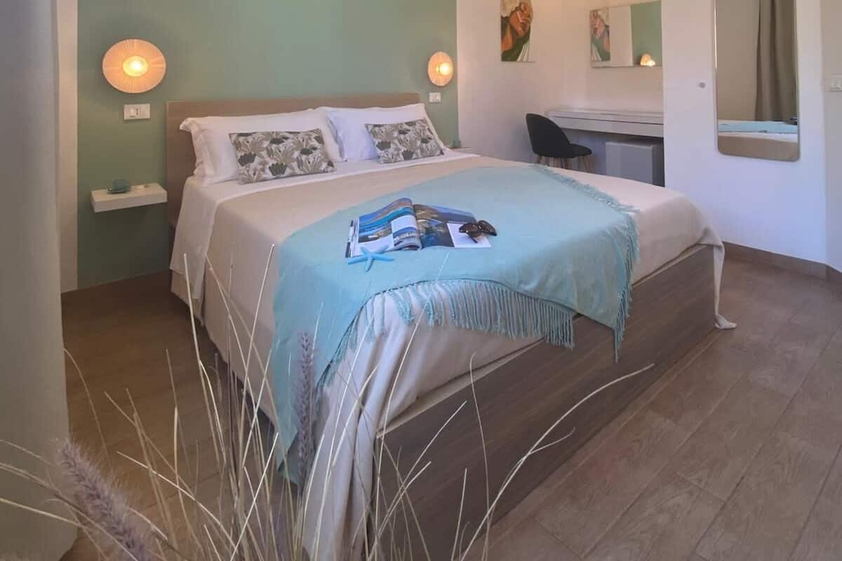 Quarto com cama, luminárias de cabeceira, espelho e lustre.