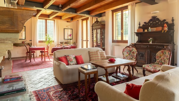 Uma sala de estar acolhedora com teto de madeira, lareira, área de jantar com mesa e cadeiras, e uma grande janela com cortinas.