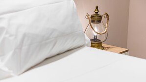 Uma cama com lençol branco e um candeeiro de latão sobre uma mesa de cabeceira de madeira.