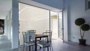 Uma área de refeições moderna com uma porta de vidro que dá para um cômodo iluminado, cadeiras de metal com almofadas e um vaso de planta.