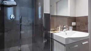Uma casa de banho moderna com chuveiro envidraçado, lavatório branco com espelho em cima e um porta-toalhas.