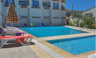 Uma piscina com espreguiçadeiras e um guarda-sol, rodeada por um edifício com varandas.