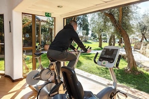 Um homem usando uma bicicleta ergométrica em um quarto com janelas amplas que dão para um jardim.