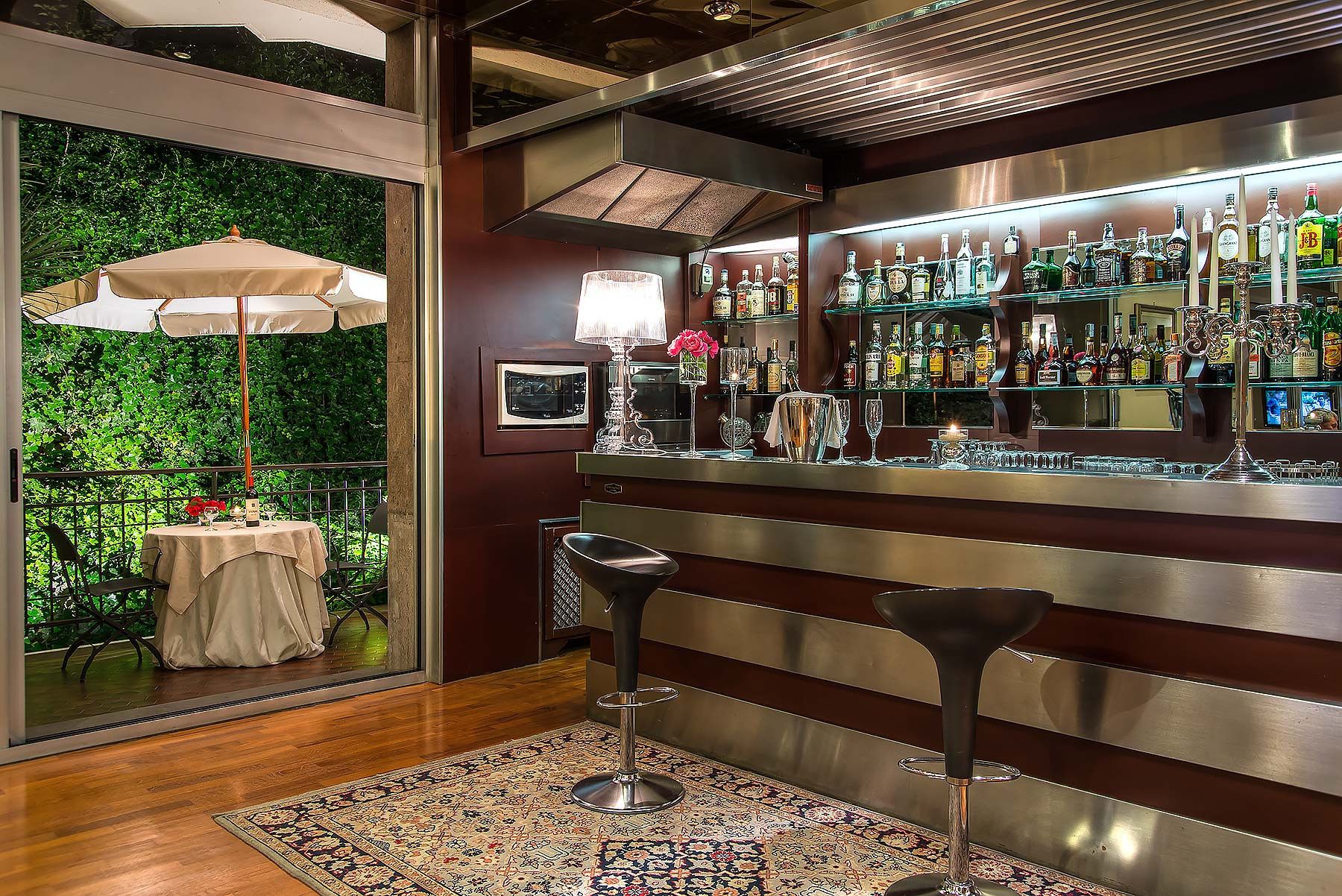 Uma área de bar com piso de madeira, tapete estampado e balcão com diversos frascos.