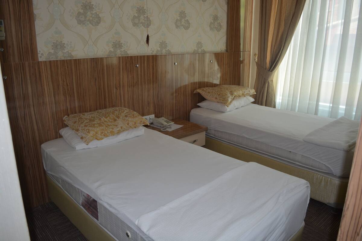 Quarto de hotel com duas camas de solteiro, cabeceira de madeira, um telefone e um espelho sobre as camas.