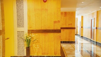 Um saguão de hotel com balcão de recepção, parede decorativa com textura e piso ladrilhado.