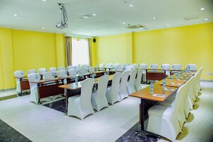 Uma sala de conferências com uma mesa comprida, cadeiras brancas e garrafas de água.