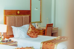 Quarto de hotel com cama, escrivaninha, cadeira, luminária e espelho.