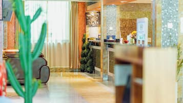 Um saguão de hotel com balcão de recepção, uma planta e área de estar.