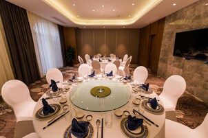 Uma sala de conferências com uma mesa de vidro redonda, cadeiras brancas e guardanapos azuis.