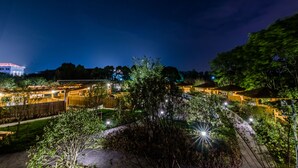Vista noturna de um resort com caminhos iluminados, estruturas de madeira e um edifício grande ao fundo.