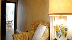 Um quarto com uma poltrona de padrão floral, uma luminária com design floral e uma cadeira de madeira ao fundo.