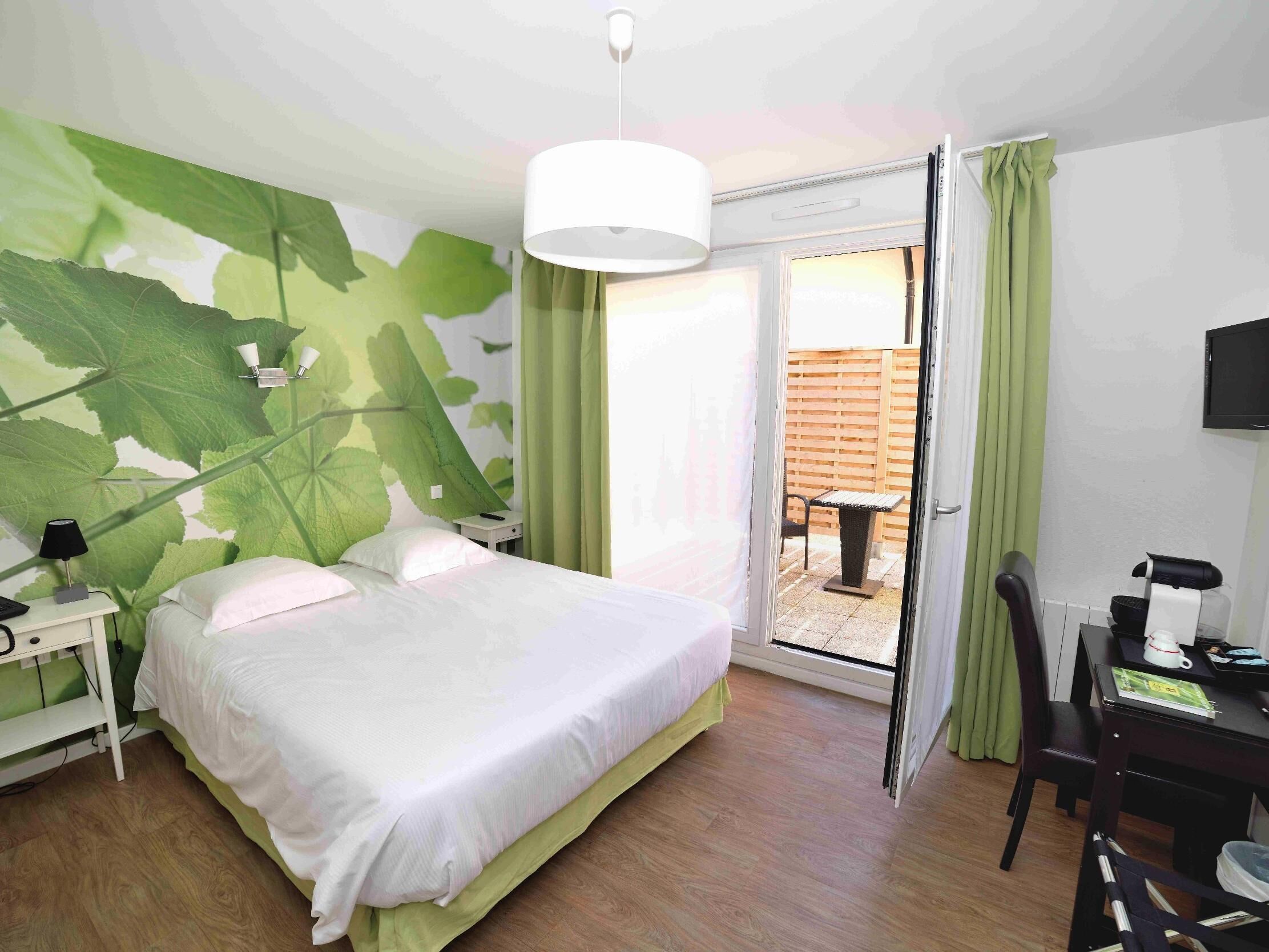Quarto com cama, mesa de cabeceira, escrivaninha, cadeira, televisão e porta de vidro corrediça para área externa.