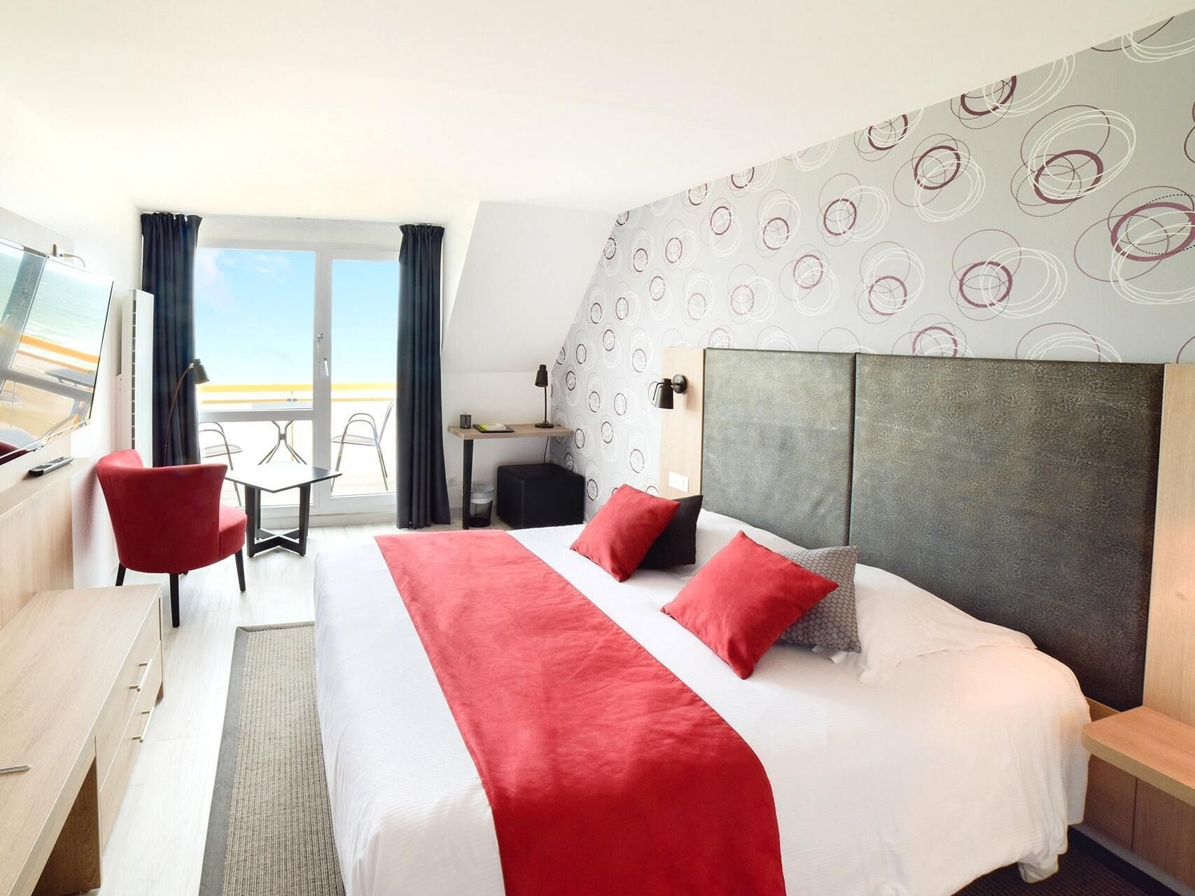 Quarto de hotel com cama, escrivaninha, cadeira, televisão e vista para o mar.
