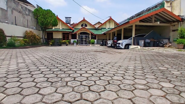 Um hotel com um pátio de azulejos hexagonais, uma área de estacionamento coberta e um edifício com telhado verde, com o nome 'Calegresco' visível.